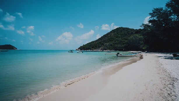 Uma praia com águas turquesa cristalinas, areal arenoso e barcos.