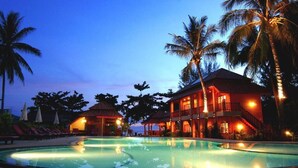 Um resort com piscina, palmeiras e um edifício com várias varandas.
