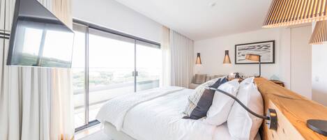 Quarto moderno com uma cama grande, cabeceira de madeira, mesa de cabeceira e vista da cidade através de janelas do chão ao teto.