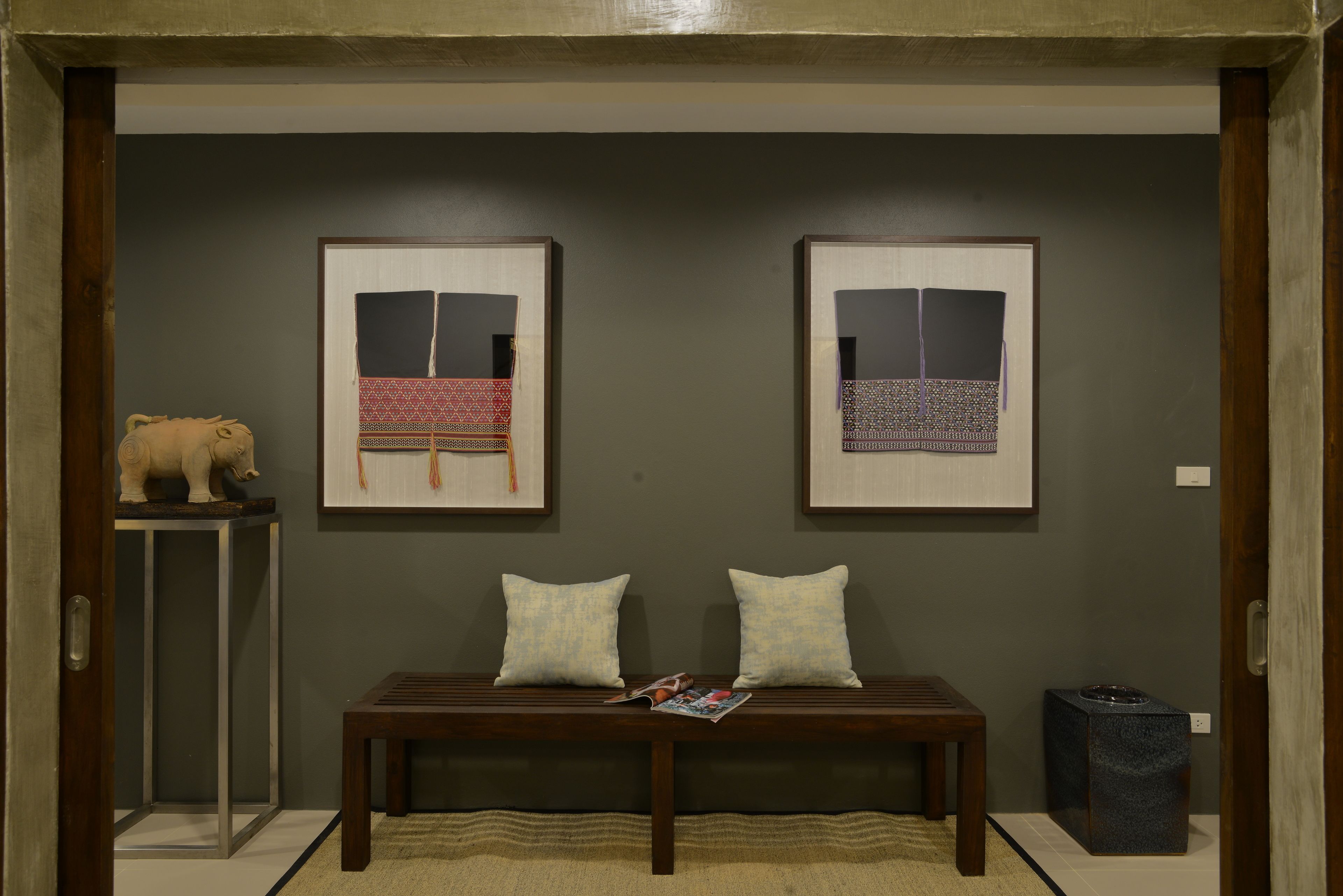 Quarto com um banco, duas almofadas, uma mesinha com uma revista e duas obras de arte emolduradas na parede.