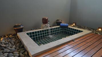 Uma banheira de hidromassagem retangular com interior revestido de azulejos, rodeada por um deck de madeira e pedrinhas.