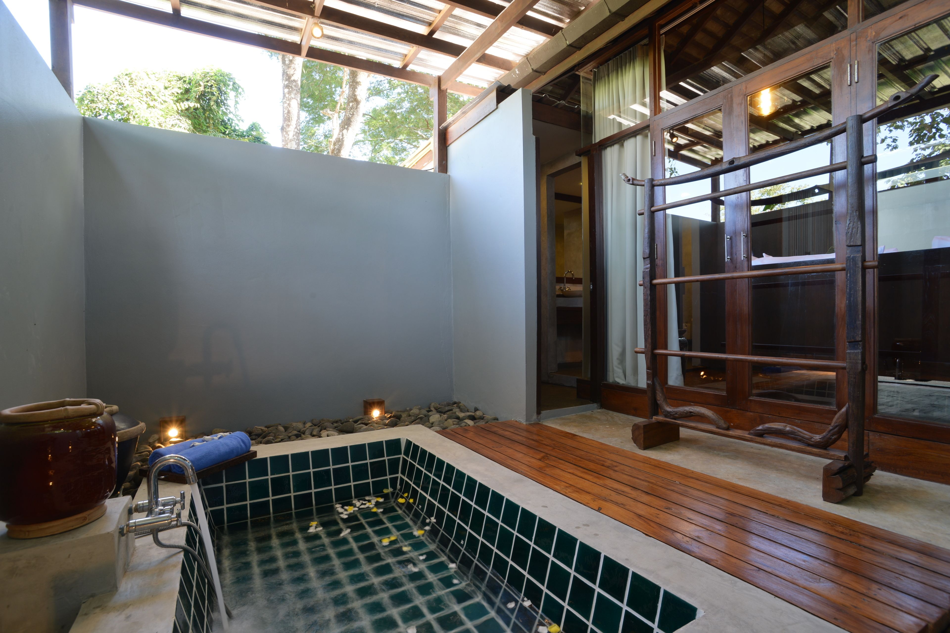 Uma área de spa com hidromassagem revestida em azulejo, deck de madeira e uma grande janela com cortinas.