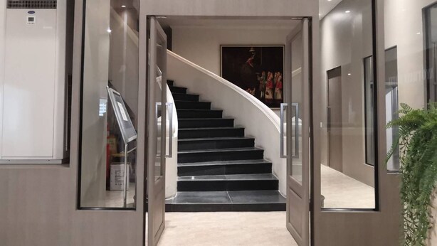 Um interior moderno com uma escada curva, portas de vidro e um cartaz na parede.