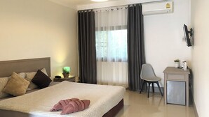 Quarto de hotel com cama, escrivaninha, cadeira, televisão e janela com cortinas.