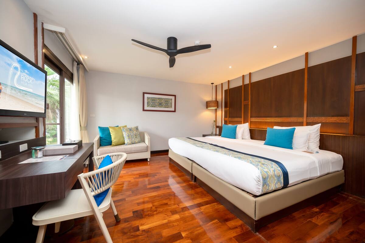Quarto de hotel moderno com uma cama grande, uma escrivaninha, uma cadeira e um ventilador de teto.