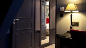 Quarto de hotel com porta fechada, uma escrivaninha com luminária e uma cadeira vermelha.