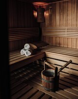 Uma sauna com bancos de madeira, um banco com toalhas e um balde de madeira.