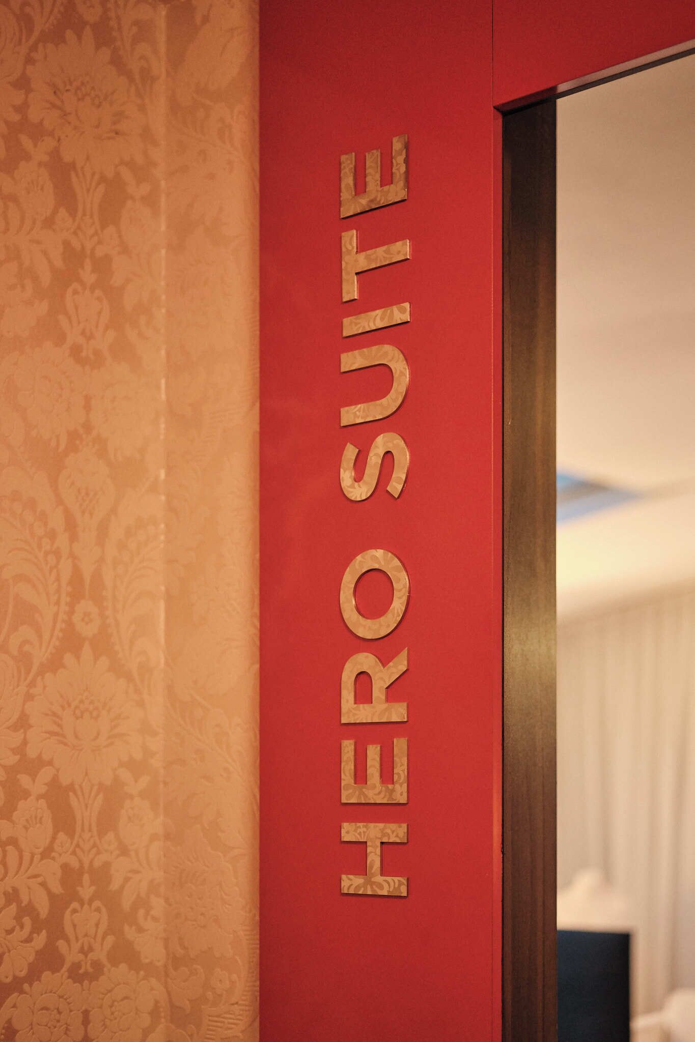 Pared vermelha com o texto 'HERO SUITE' em letras douradas.