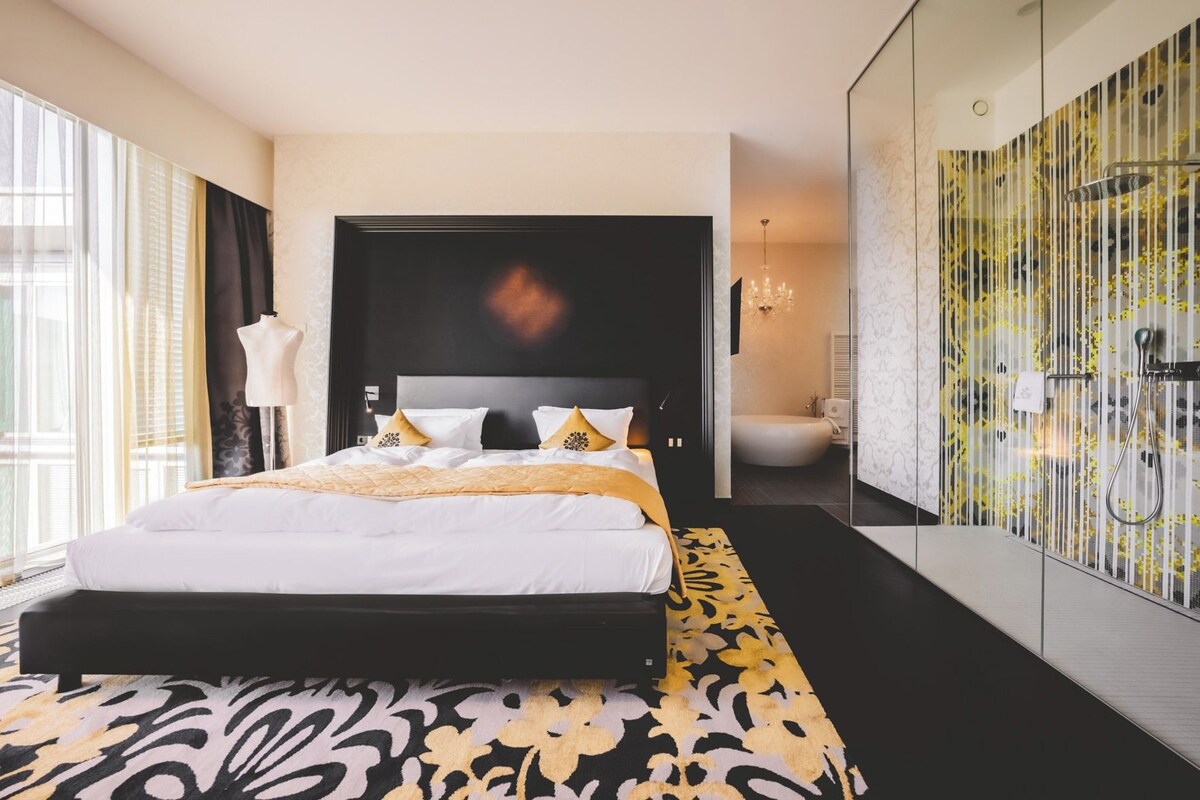 Quarto de hotel moderno com uma cama grande, banheiro separado e vista para a cidade.