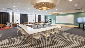 Uma sala de conferências com uma mesa grande, cadeiras, tela de projetor e quadro branco.