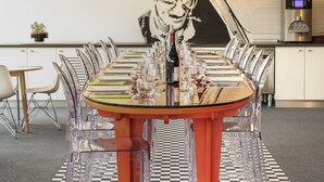 Uma sala de conferências com piso xadrez, uma mesa redonda com cadeiras e um grande lustre vermelho no teto.