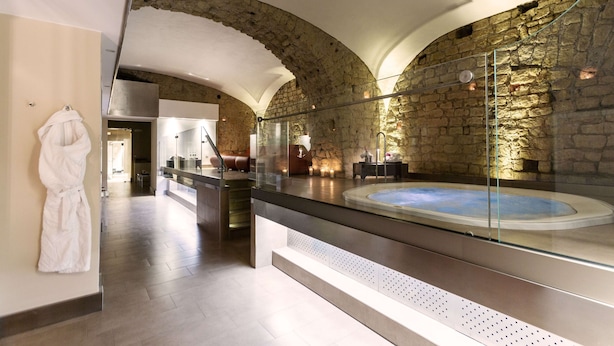 Uma área de spa moderna com parede de pedra, hidromassagem em vidro e um roupão pendurado na parede.