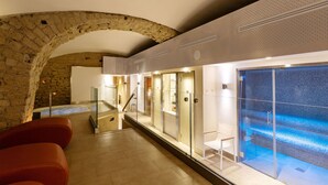 Interior moderno com um arco de pedra, área de spa com paredes de vidro e escadaria que leva aos andares superiores.
