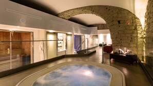 Um hall amplo com uma banheira de hidromassagem central, um arco de pedra e uma área de recepção moderna.