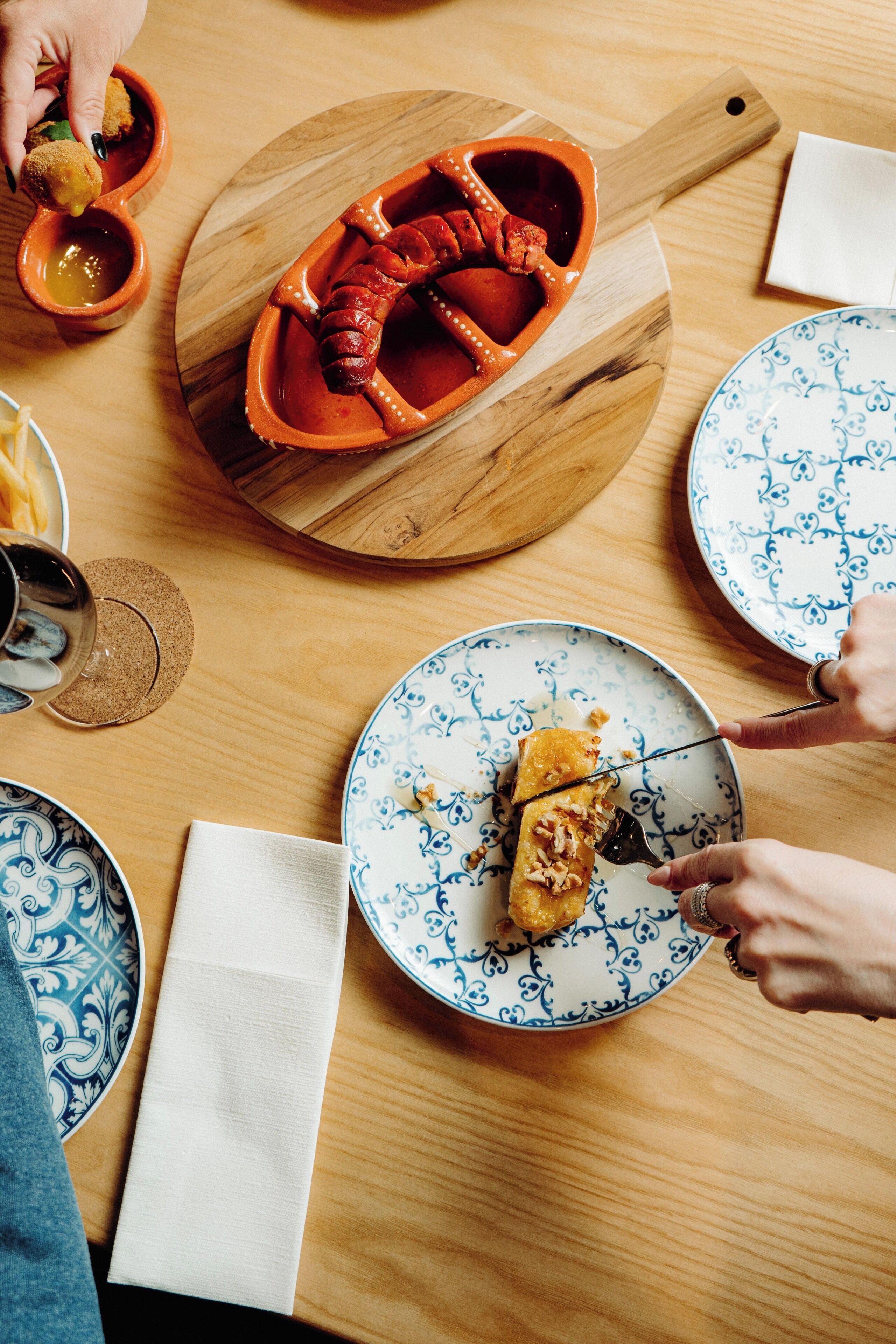 Uma mesa de madeira com vários pratos, incluindo um prato com um pedaço de comida e uma tigela de salsichas.