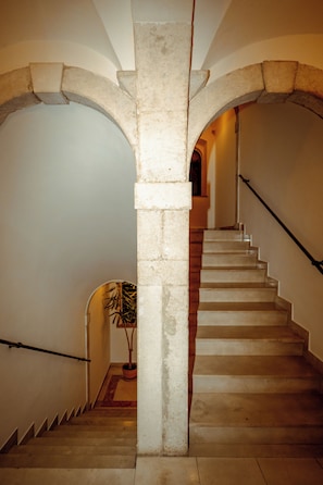 Uma escadaria com arcos de pedra e corrimão, que dá acesso a um andar superior.
