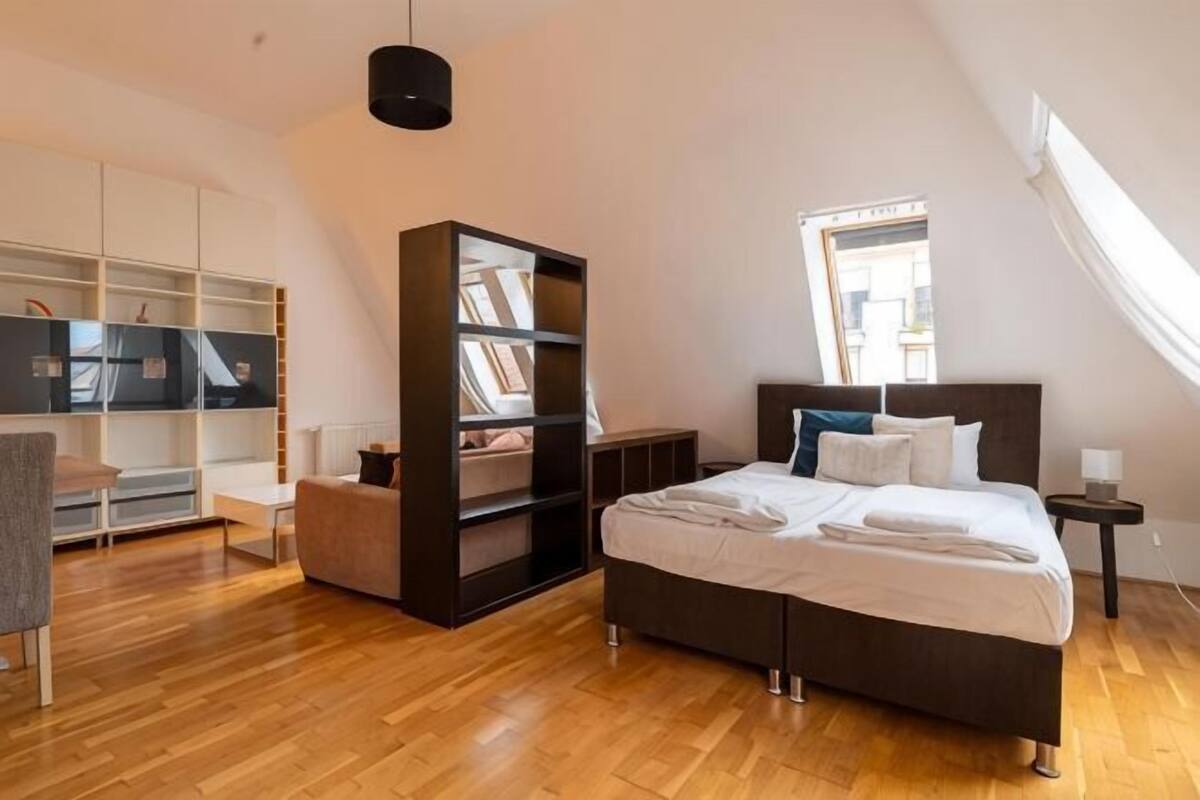 Um quarto com uma cama, uma estante, uma escrivaninha e uma janela.
