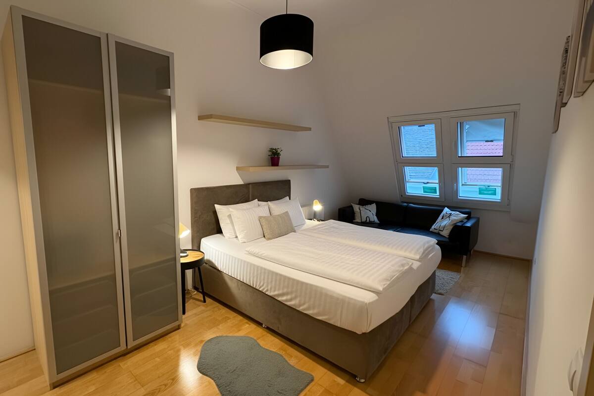 Quarto com cama, mesa de cabeceira, escrivaninha, janela e porta deslizante.
