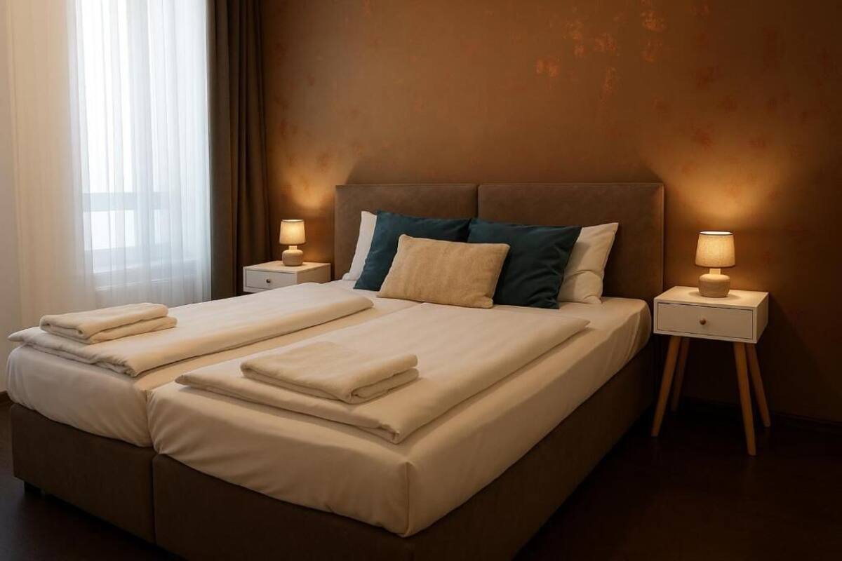 Cama de casal com cabeceira, duas mesas de cabeceira com abajures e uma janela com cortinas.
