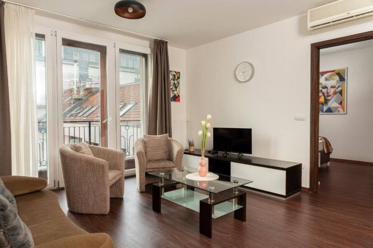 Uma sala de estar moderna com uma mesa de centro de vidro, duas poltronas, um sofá, uma televisão de tela plana e um console de mesa minimalista.