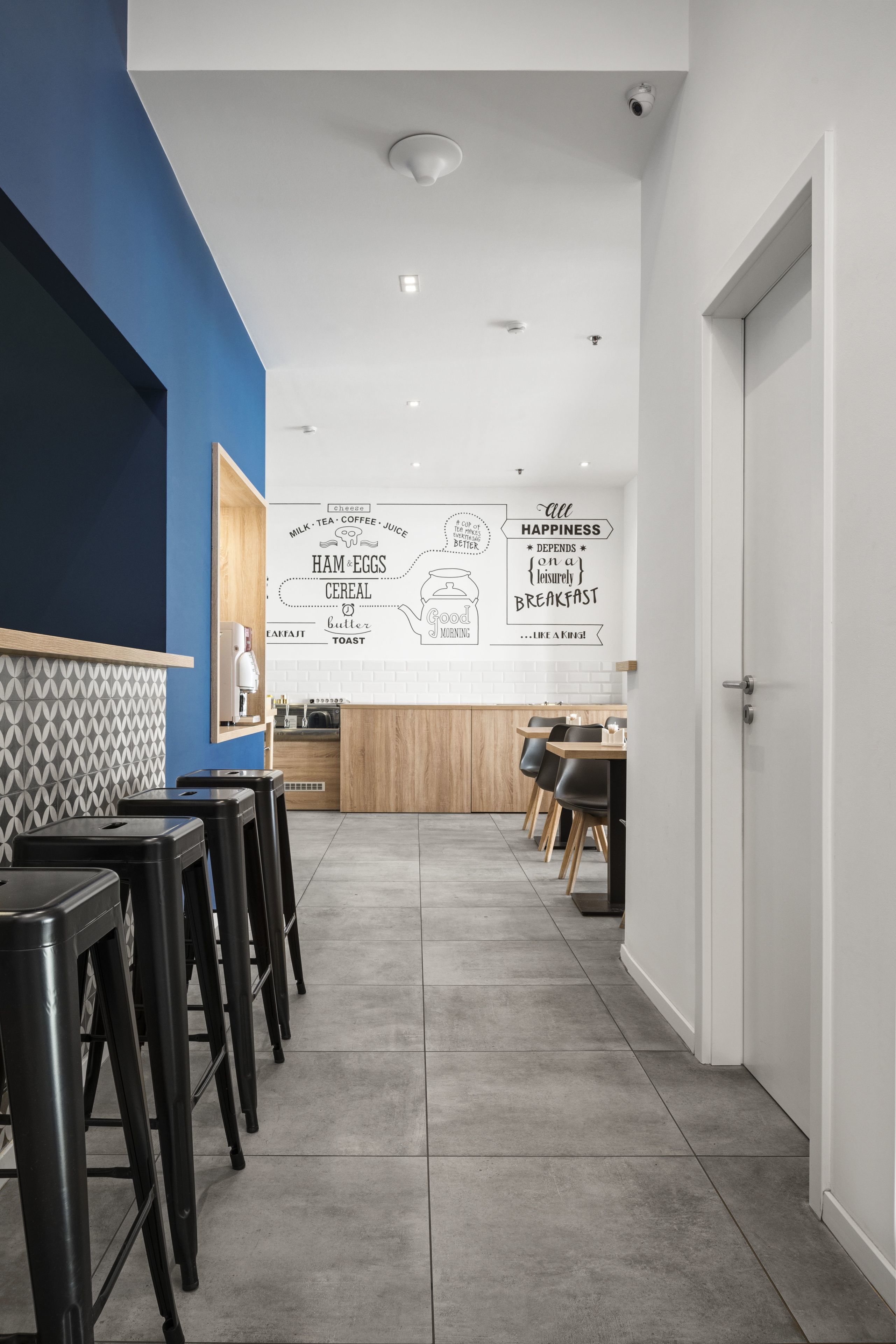 Uma cozinha moderna com balcão de refeições, cafeteira e parede decorada com ilustrações sobre o café da manhã.