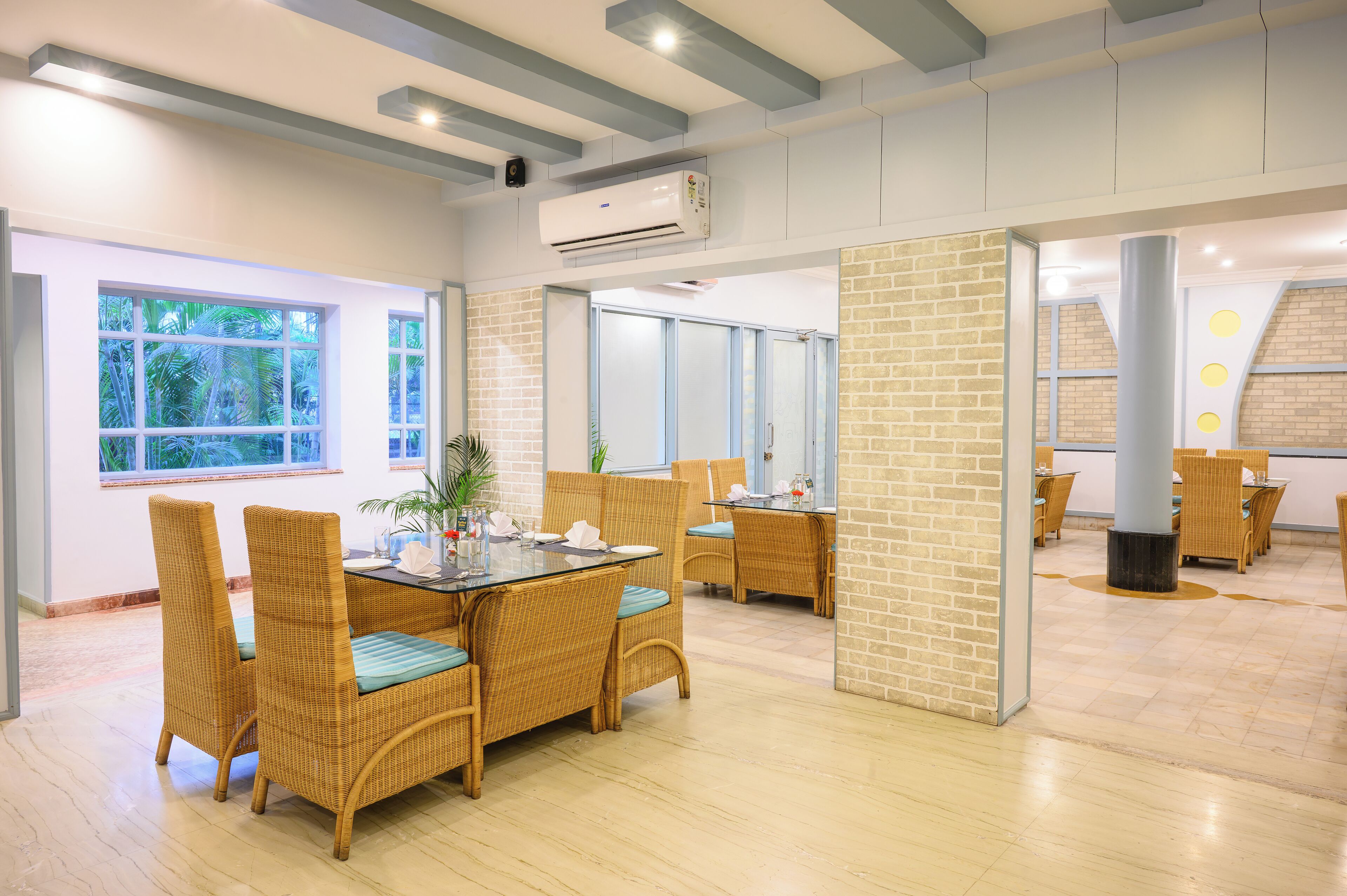 Uma sala de jantar com mobiliário de vime, janelas amplas e uma parede de destaque em tijolo.