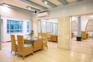 Uma sala de jantar com mobiliário de vime, janelas amplas e uma parede de destaque em tijolo.
