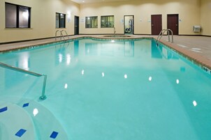 Piscina interior com água cristalina, rodeada por paredes e portas bege.