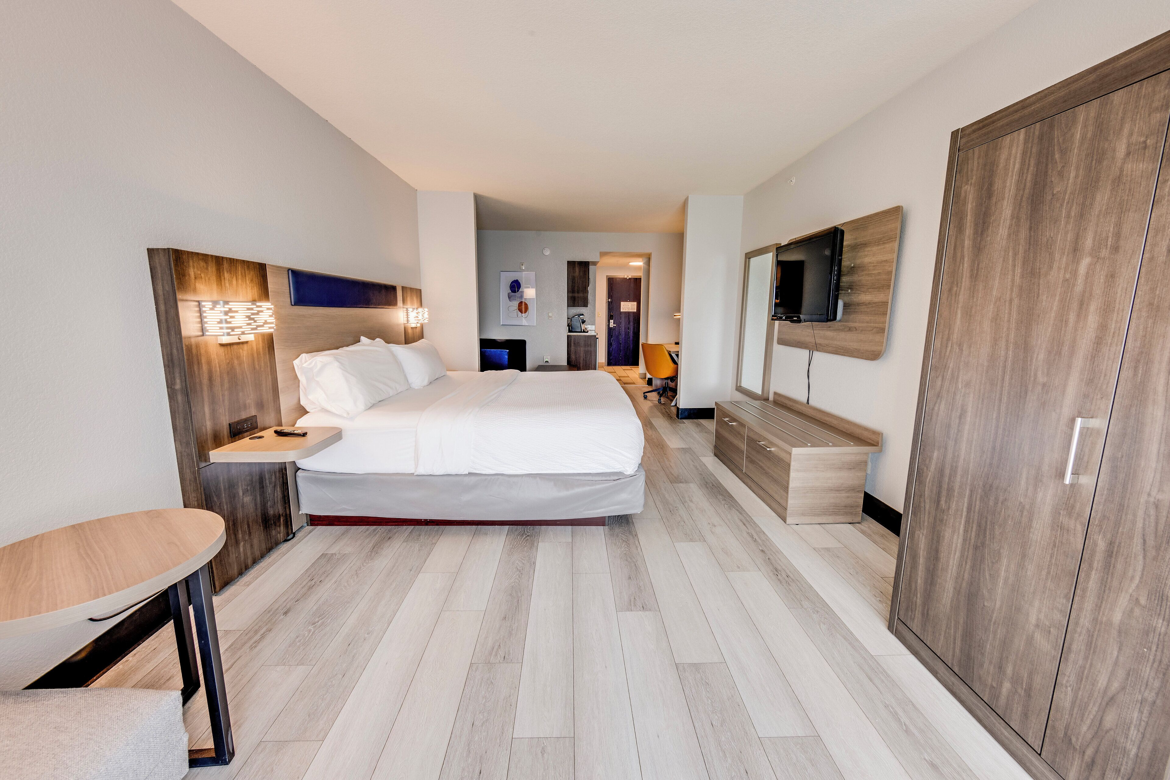 Quarto de hotel moderno com uma cama grande, uma escrivaninha, uma TV na parede e um guarda-roupa.