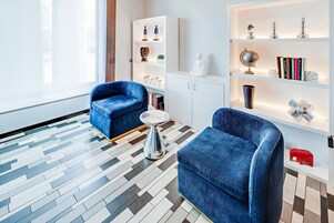 Uma sala de estar moderna com dois poltronas azuis, uma estante branca e um piso estampado.