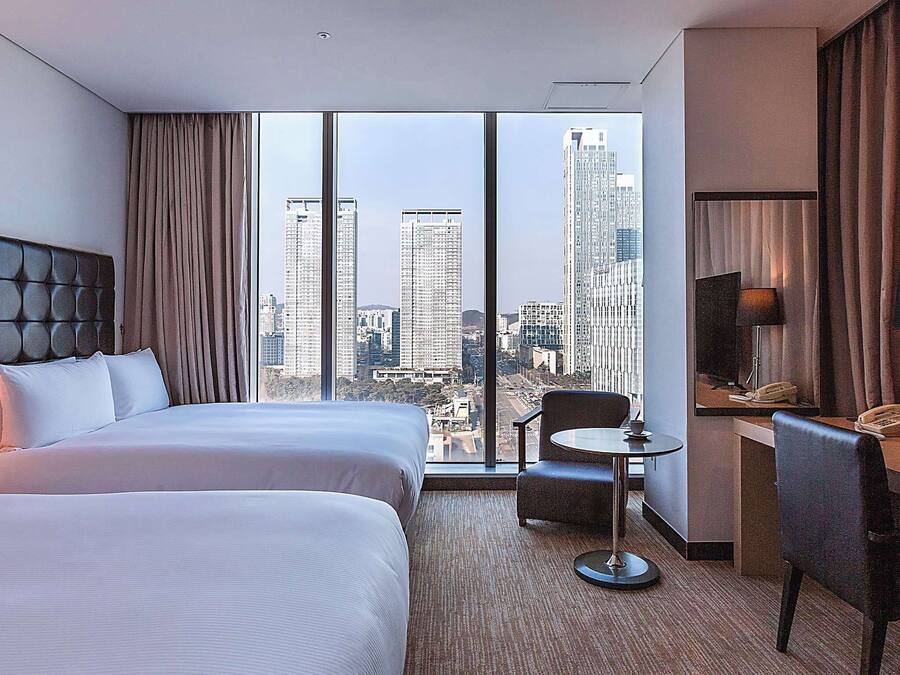 Quarto de hotel com duas camas, uma escrivaninha, uma cadeira, televisão e vista para a cidade.