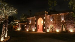 Um edifício histórico com arcadas iluminadas e janelas, rodeado por palmeiras.
