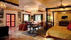 Um quarto espaçoso com uma cama de dossel, um espaço de refeições e uma área de estar com um candelabro.