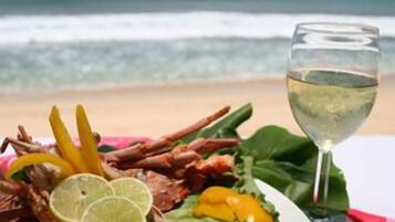 Prato de mariscos com fatias de limão e rabanetes, um copo de vinho branco e vista para o oceano.
