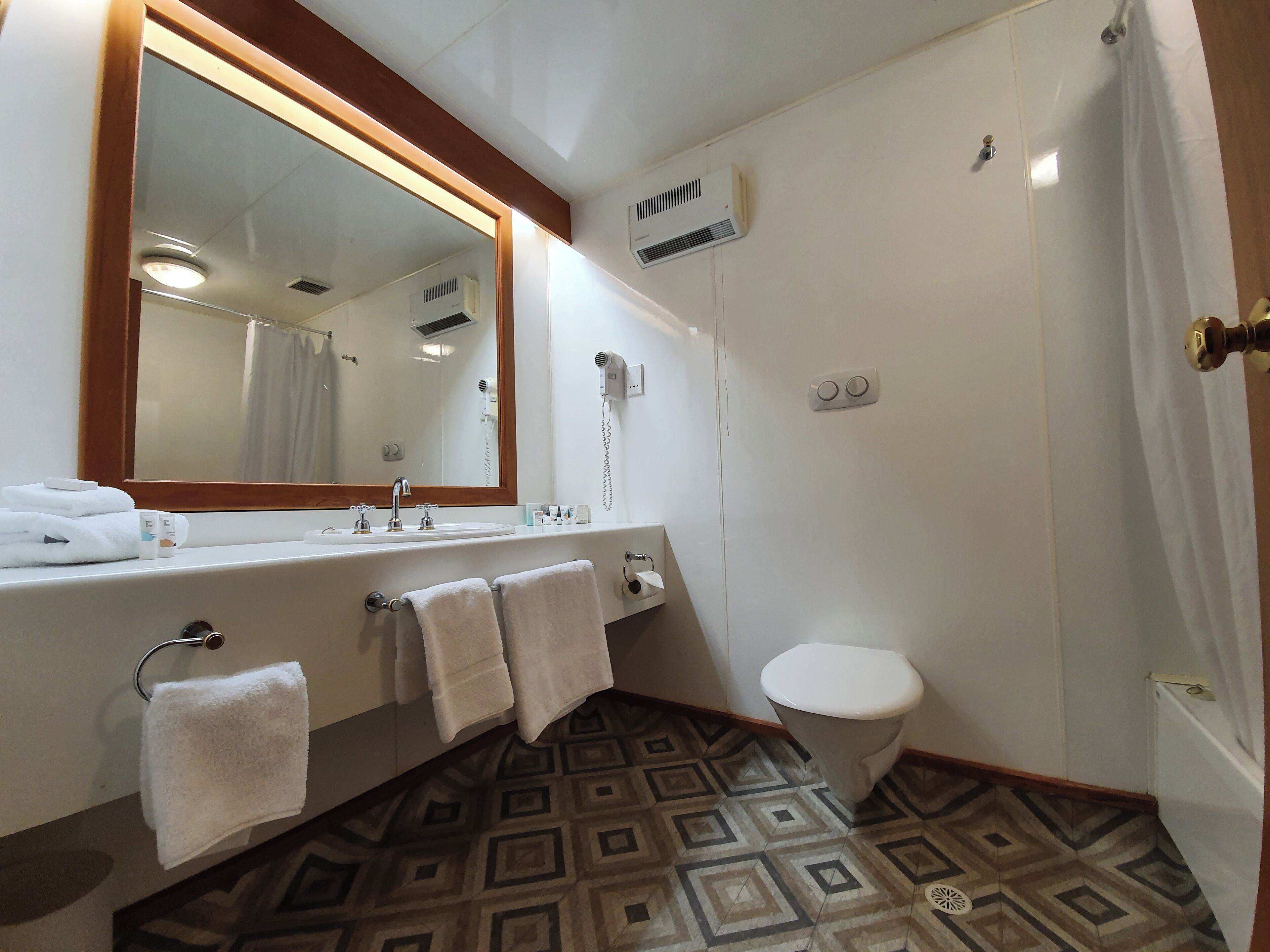 Casa de banho com lavatório, espelho, porta-toalhas, sanita e chão estampado.