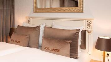 Quarto de hotel com cama, almofadas, mesa de cabeceira, abajur e espelho na parede.