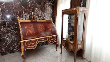 Um quarto com parede de mármore, um banco ornamentado em vermelho e dourado, e um armário de madeira com portas de vidro.