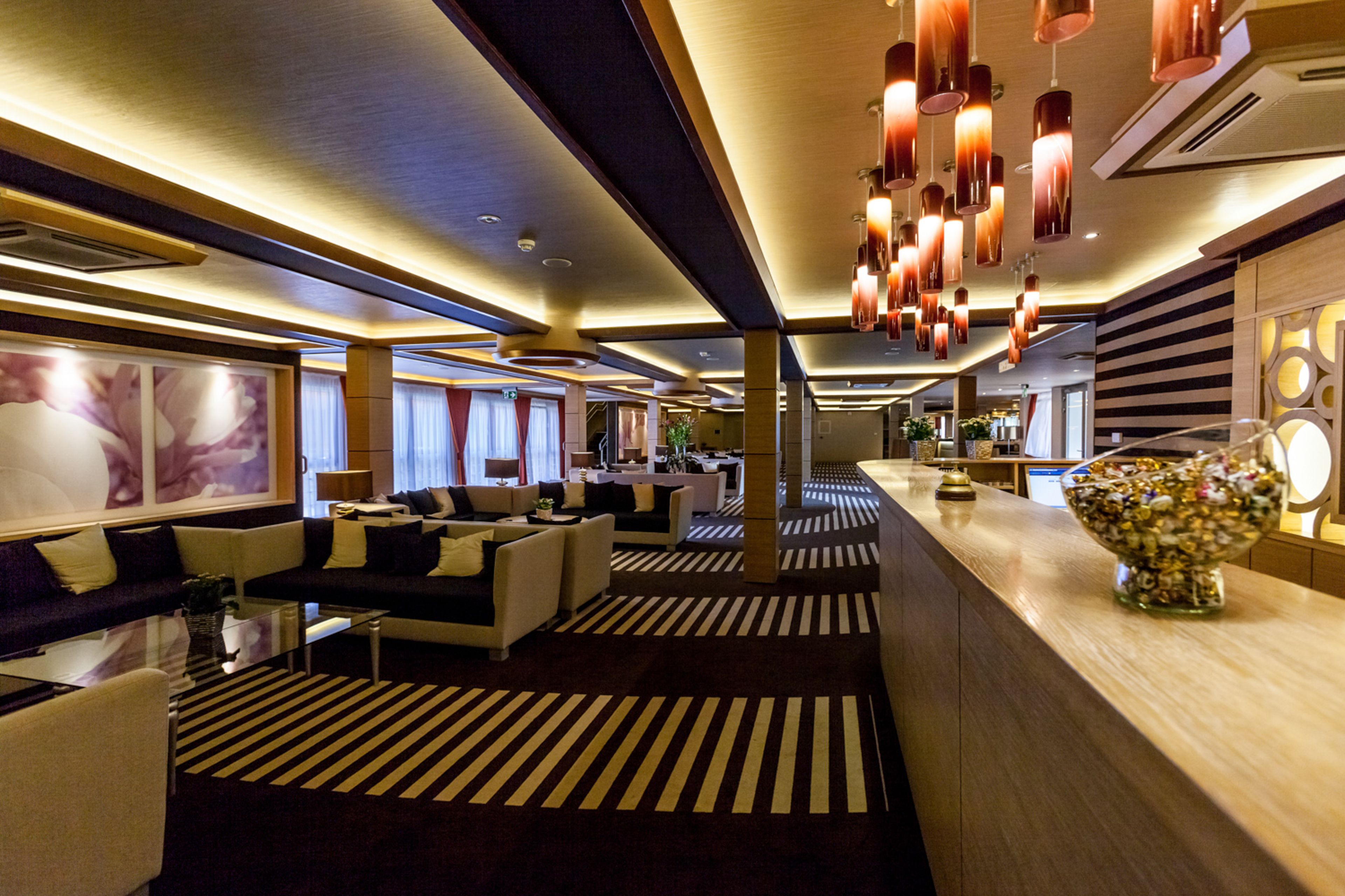 Um lobby de hotel moderno com balcão de recepção, sofás e um tapete listrado.