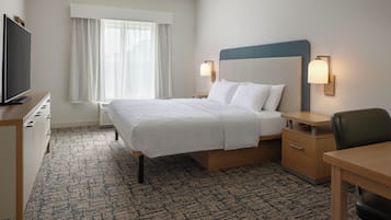 Quarto de hotel com cama, mesas de cabeceira, escrivaninha, cadeira, televisão e janela com cortinas.