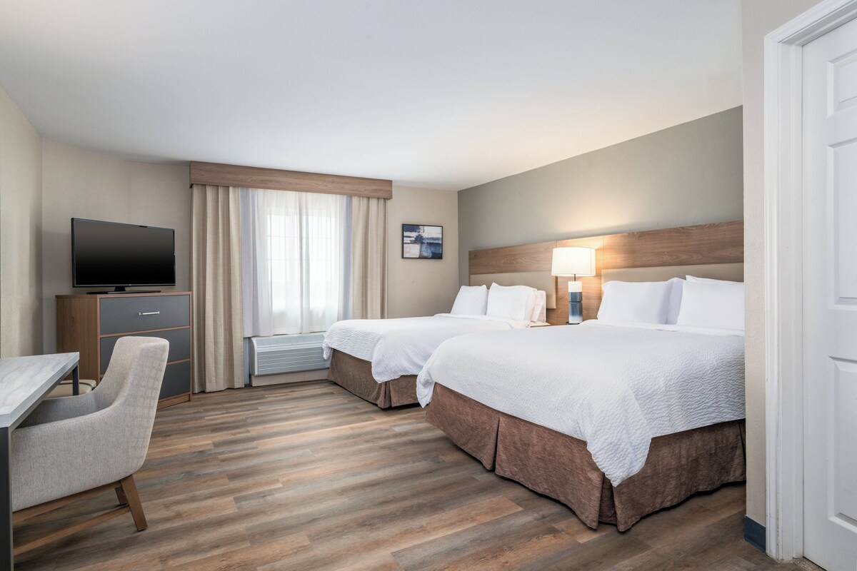 Quarto de hotel com duas camas, uma escrivaninha, uma televisão e uma janela com cortinas.