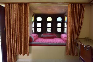 Quarto com cama, cortinas e janela com vidro decorativo.