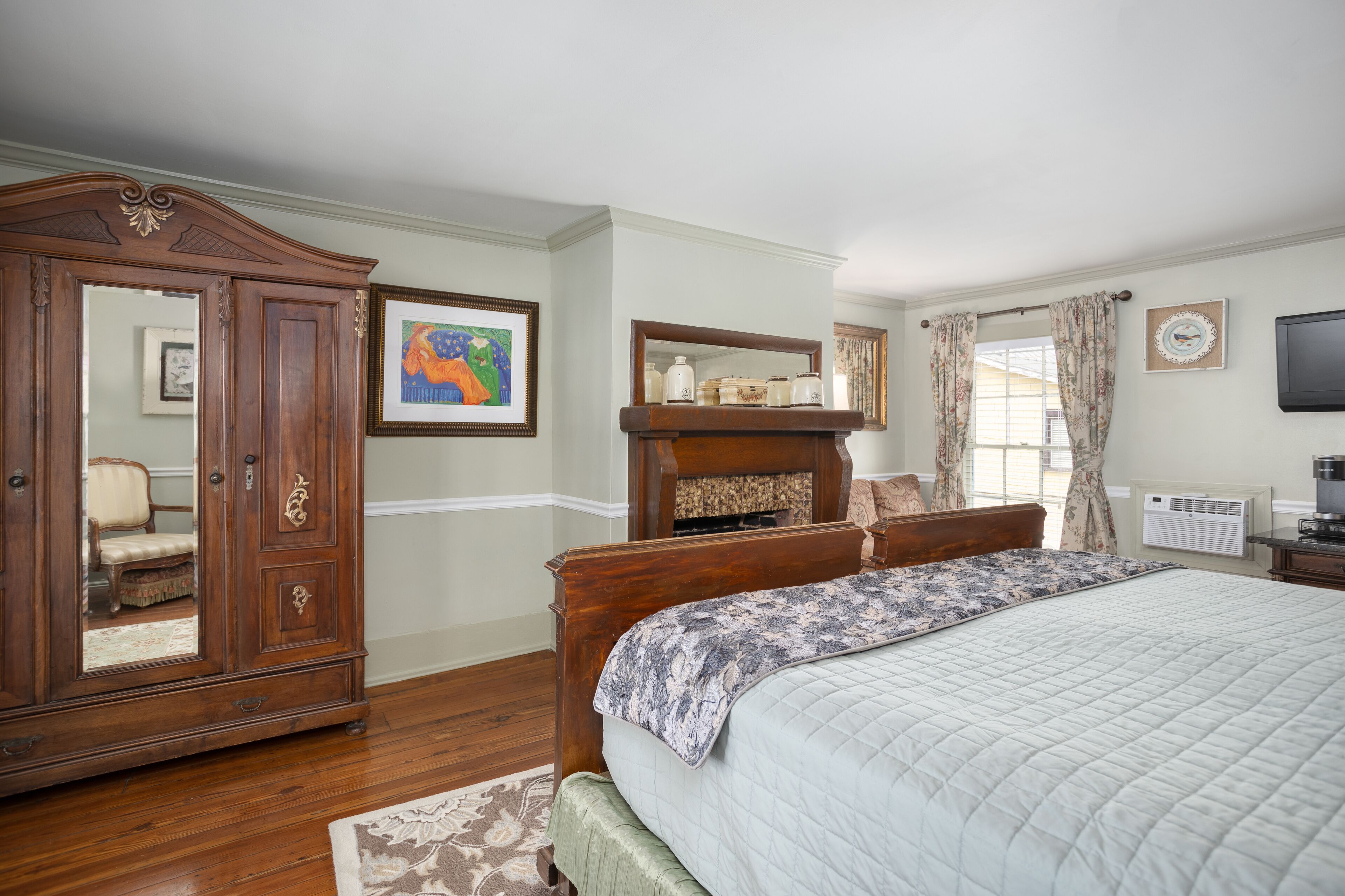 Quarto com cama grande, guarda-roupa de madeira, espelho, quadro emoldurado e televisão.