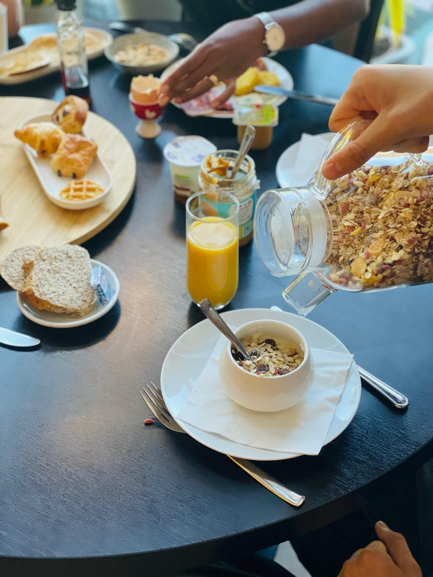 Mesa posta para o café da manhã, com tigela de cereal, copo de suco de laranja e diversos alimentos.