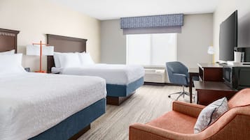 Quarto de hotel com duas camas, uma escrivaninha com televisão de tela plana, uma cadeira e um sofá.