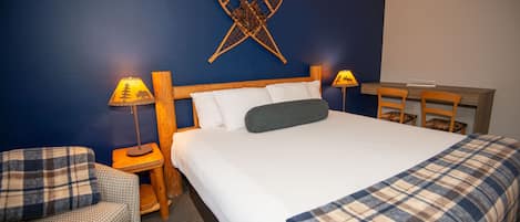 Quarto de hotel bem arrumado com uma cama grande, duas mesas de cabeceira com abajures, uma escrivaninha de madeira e uma cadeira.