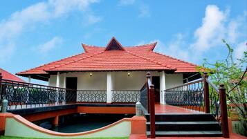 Um edifício com telhado de telhas vermelhas, uma escadaria com corrimão e uma pequena área de piscina.