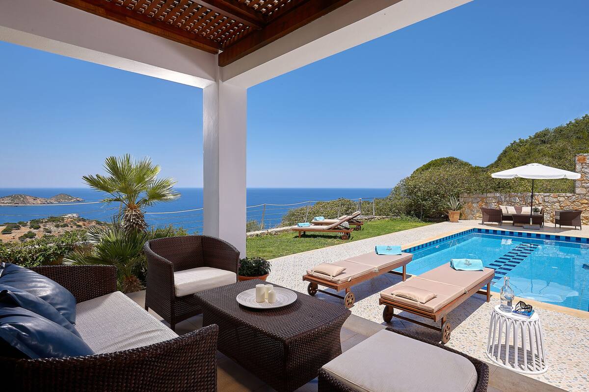 Uma área à beira da piscina com móveis de vime, vista para o mar e céu claro.