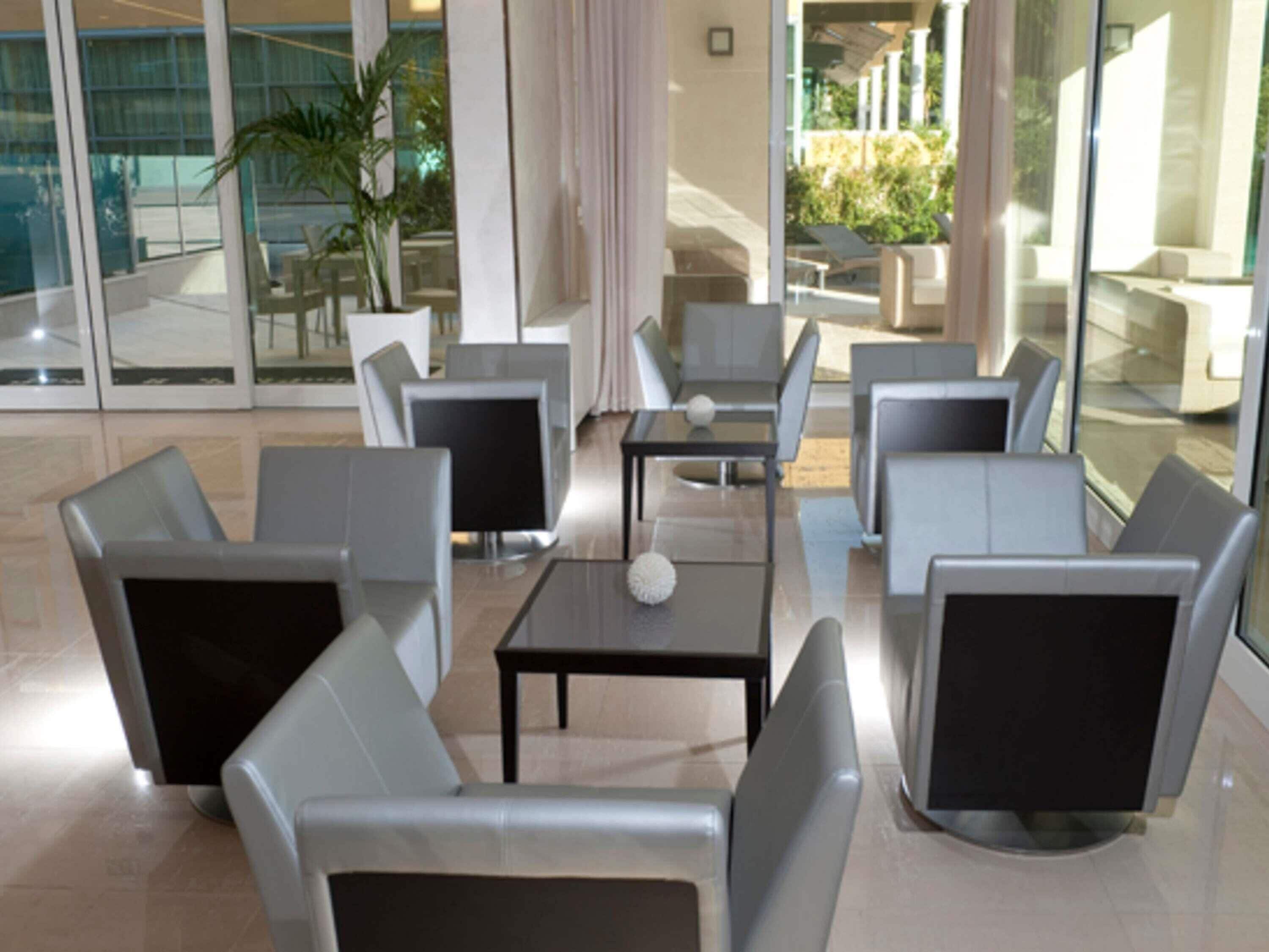 Uma área de estar moderna, com assentos e uma mesa, janelas amplas e vista para um espaço ao ar livre.