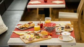 Uma mesa de café da manhã com diversos alimentos, um copo de suco de laranja e uma xícara de café.
