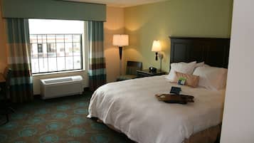 Quarto de hotel com uma cama grande, uma escrivaninha, uma cadeira, um abajur e uma janela com cortinas.